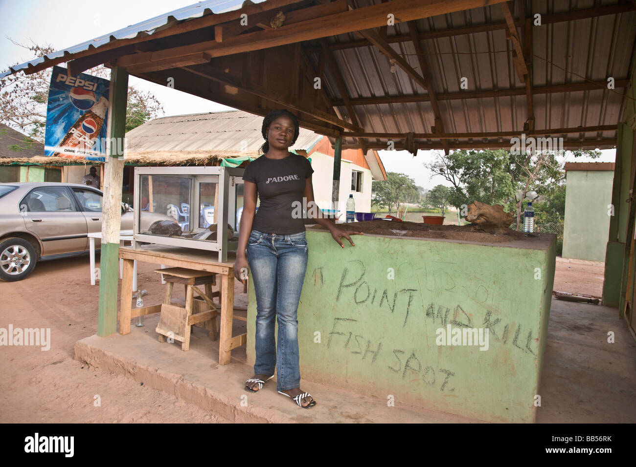 A young woman grills fish at a roadside "point and kill" fish stand in ...