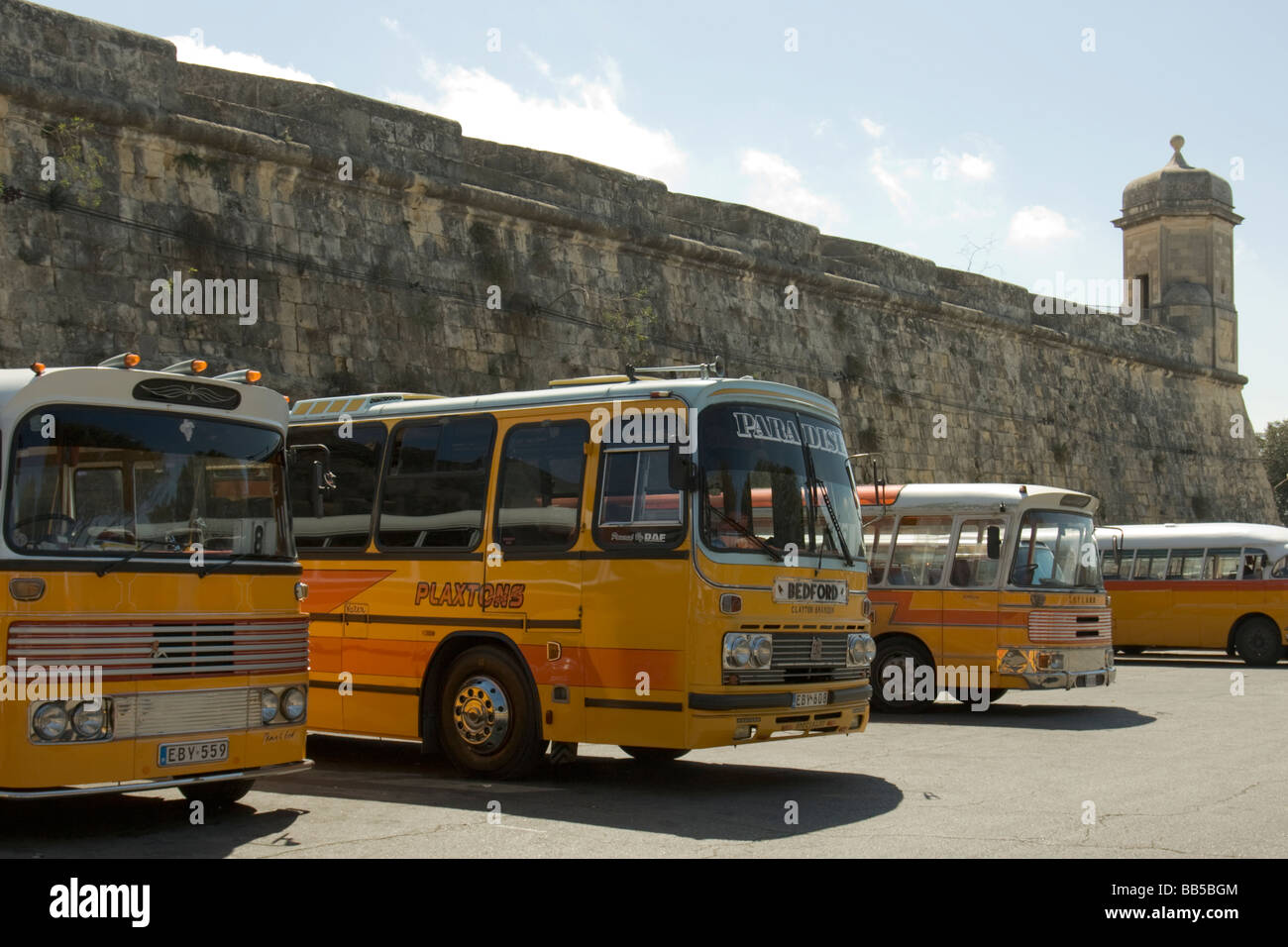 A line of bright yellow Maltese buses parked in a bus station alongside ...