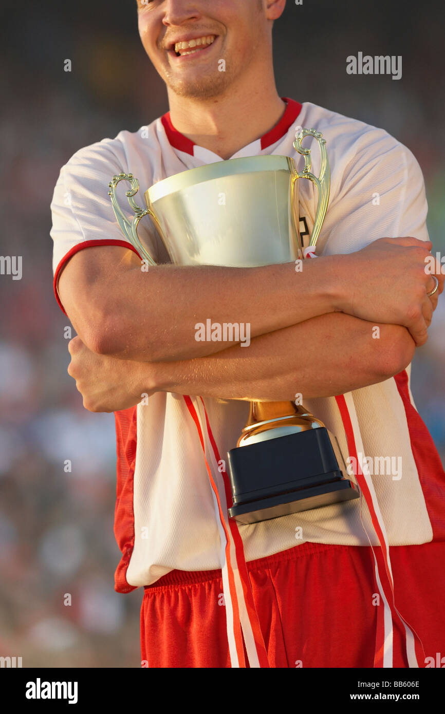 Male soccer player triumphantly hugging trophy Stock Photo - Alamy