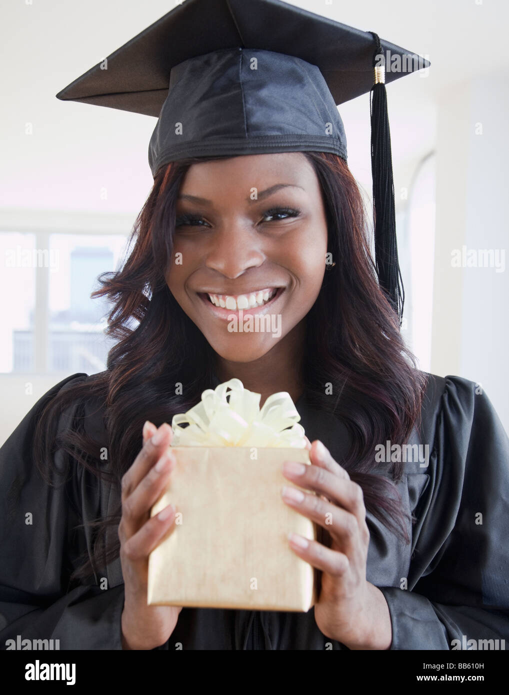 African woman in graduation cap and gown holding gift Stock Photo - Alamy