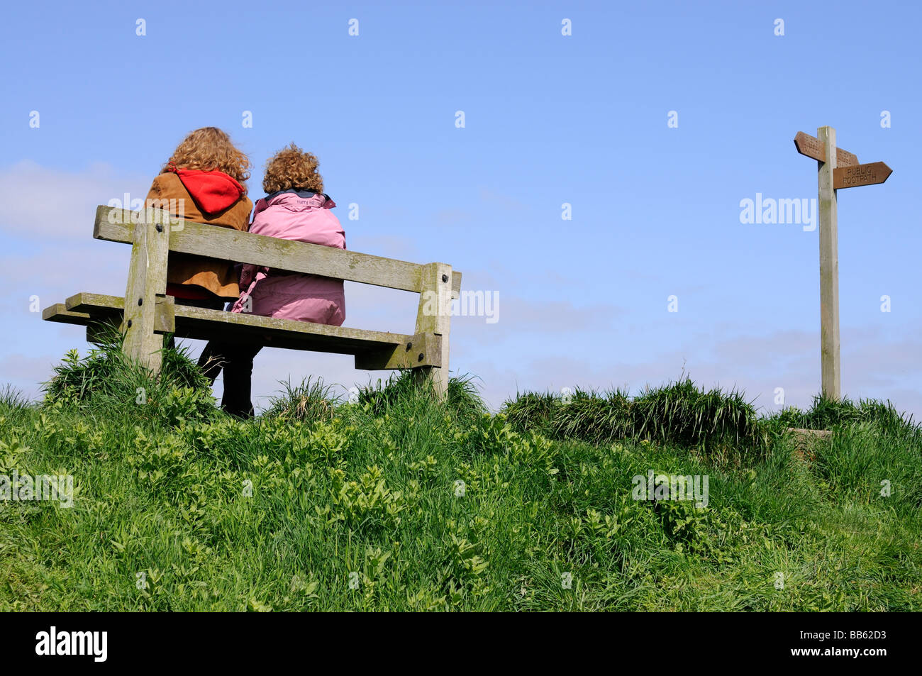 Two Female Walkers Resting on a Bench, Close to a Signpost, on a Bright ...