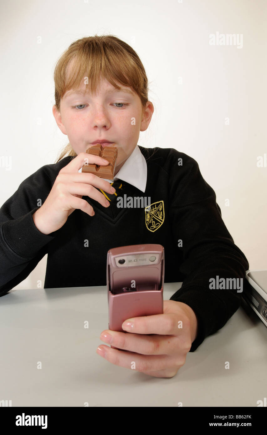 Schoolgirl eating a chocolate bar and using her mobile phone Stock ...