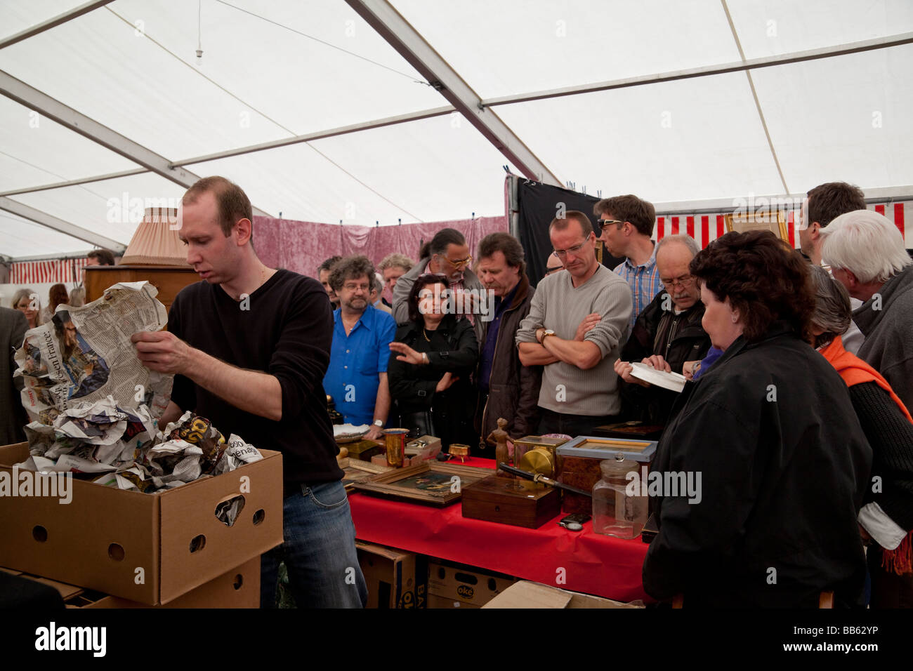 A group of people gather around a booth at the antique market in ...