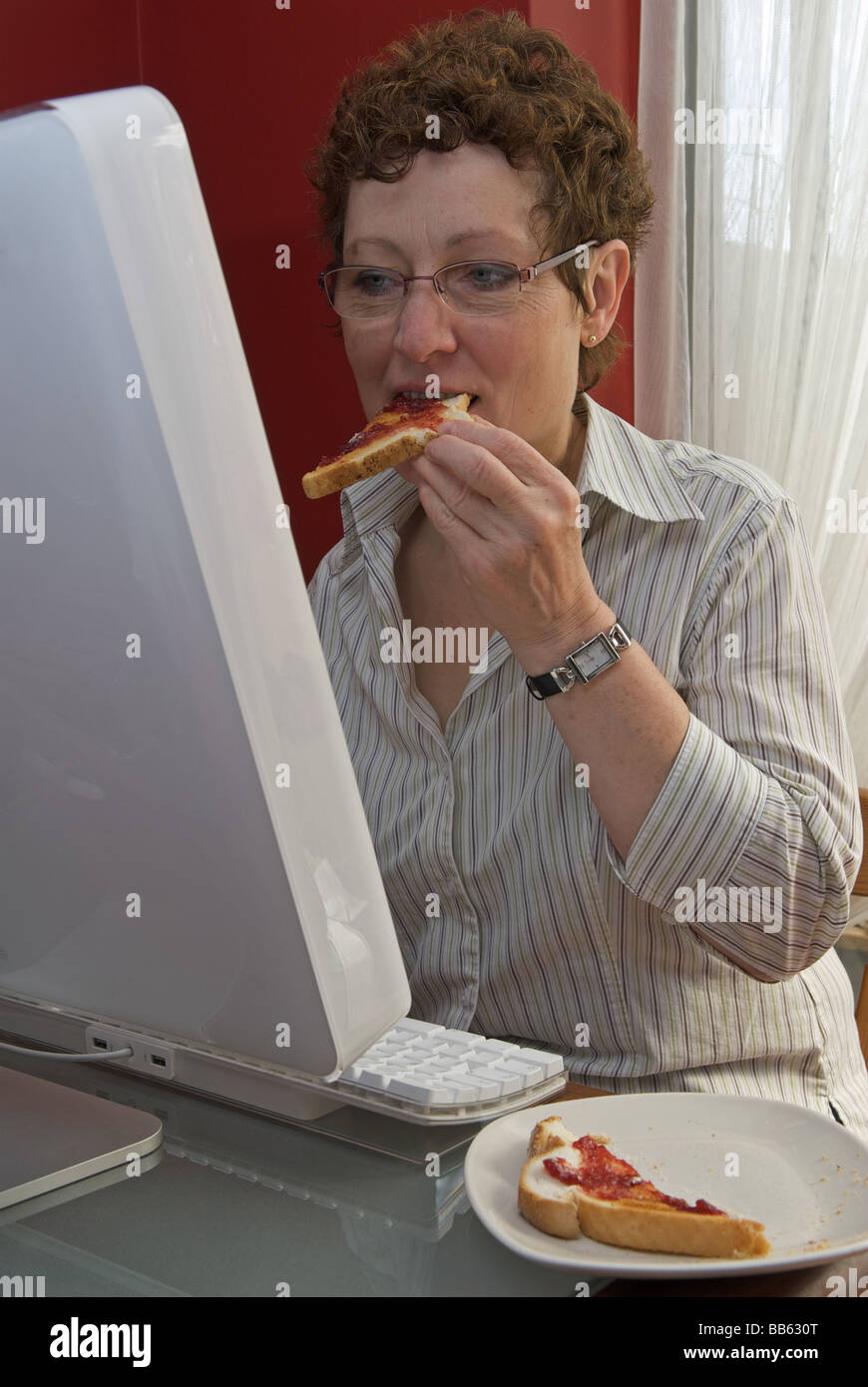 Woman eating breakfast while working from home on a computer Stock ...