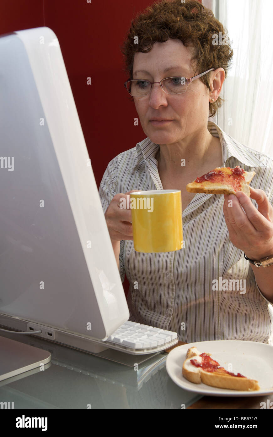 Woman eating breakfast while working from home on a computer Stock ...