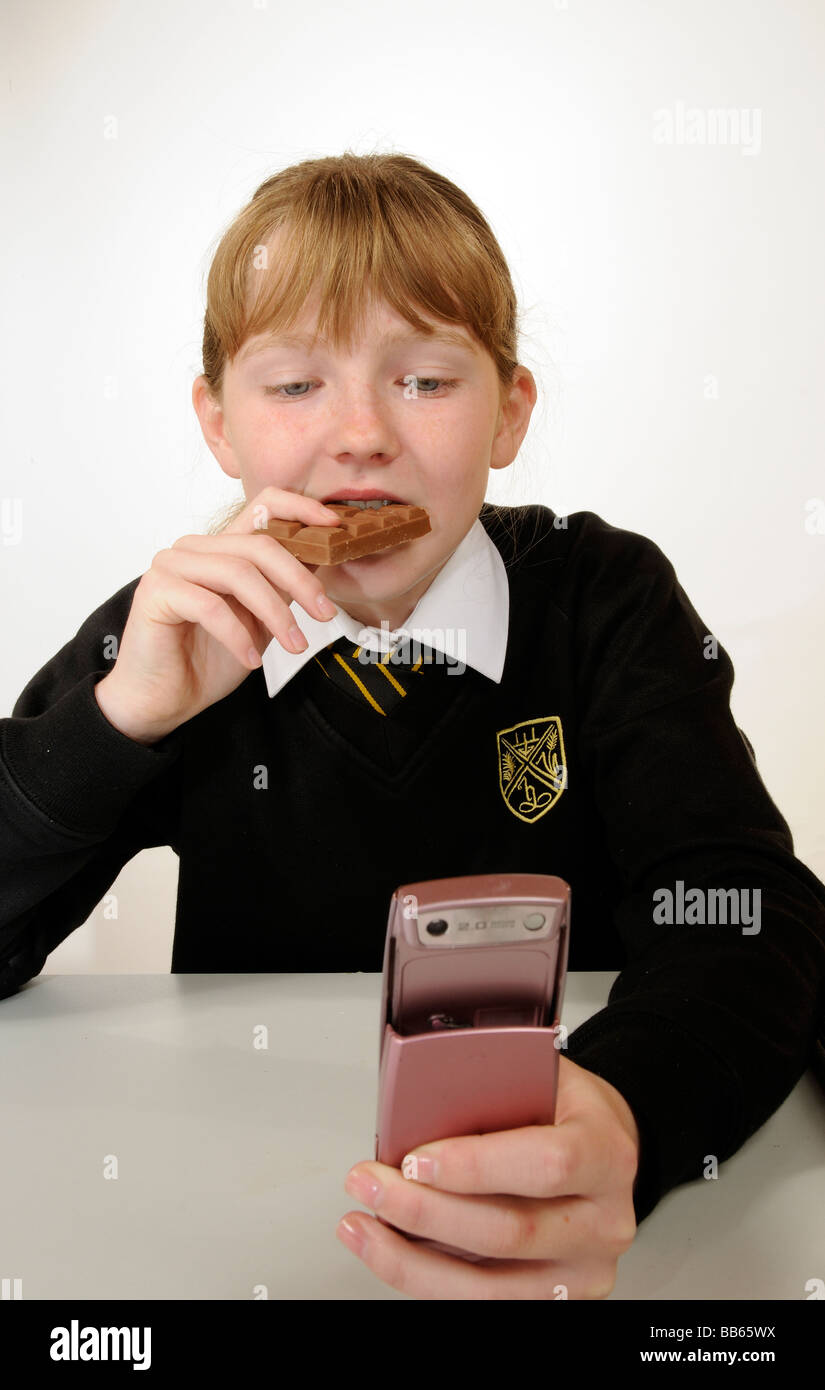 Schoolgirl eating a chocolate bar and using her mobile phone Stock ...