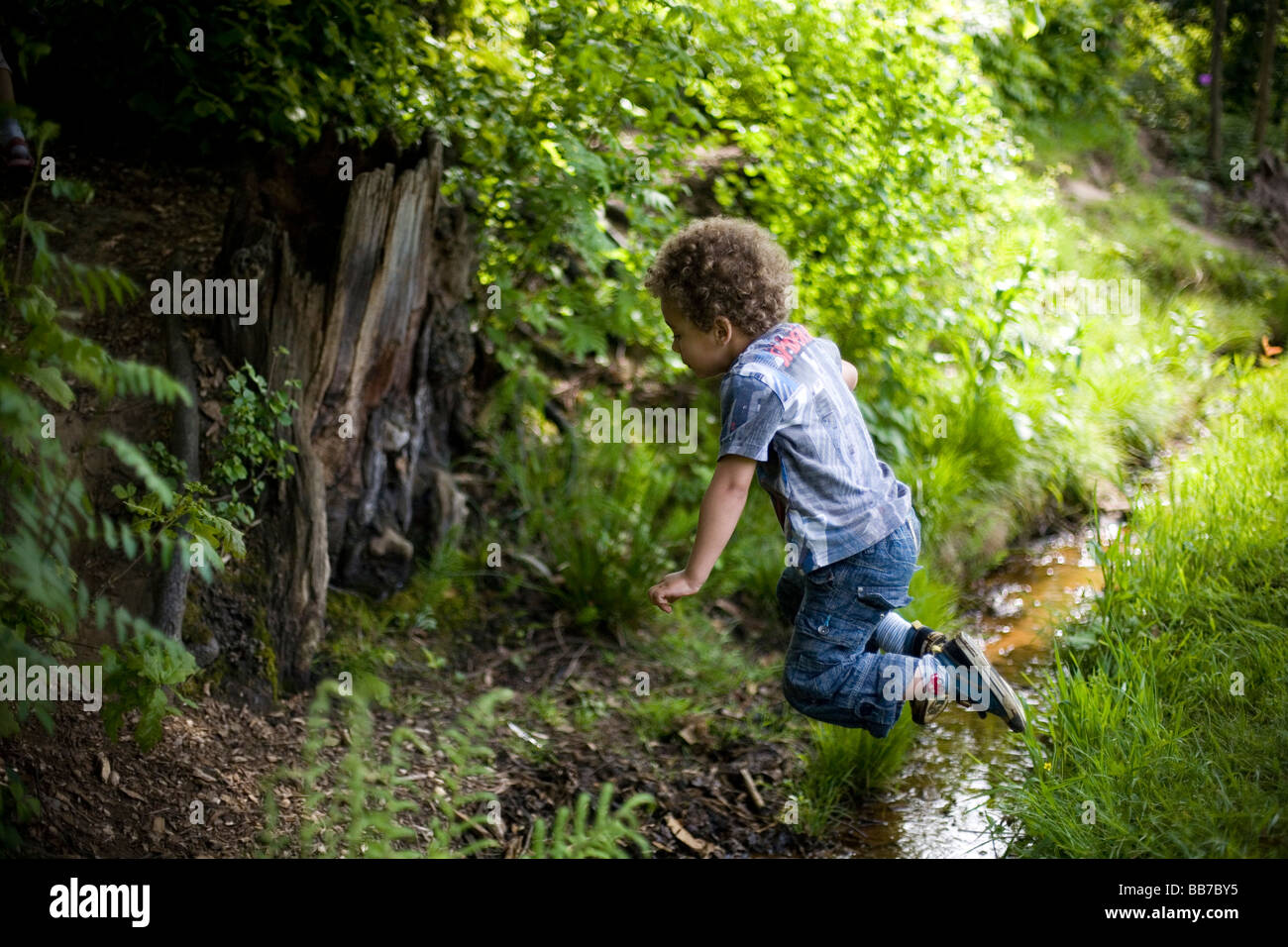 Young boy jumping across stream Stock Photo - Alamy