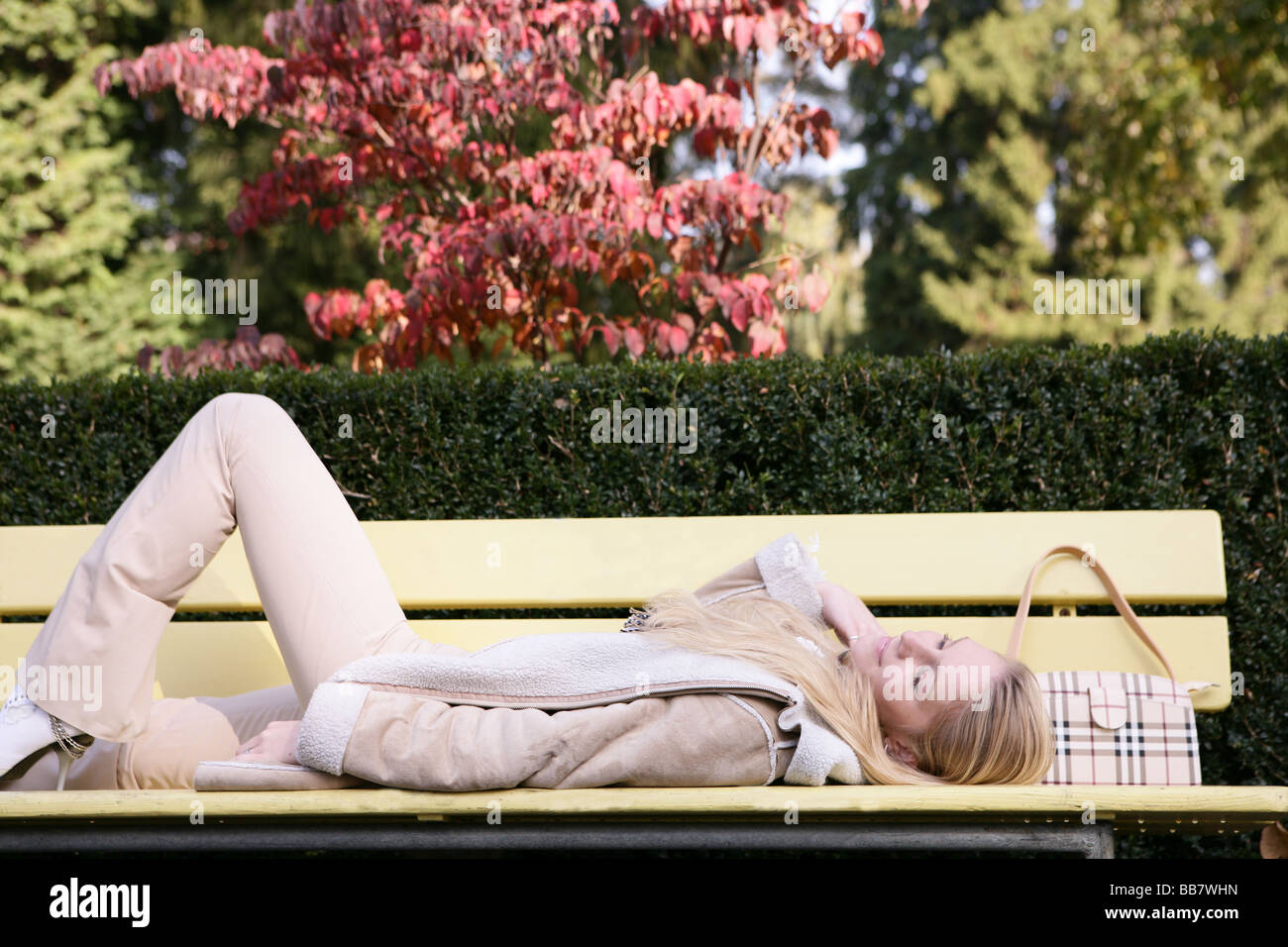 a woman is lying on a bench in a park Stock Photo - Alamy