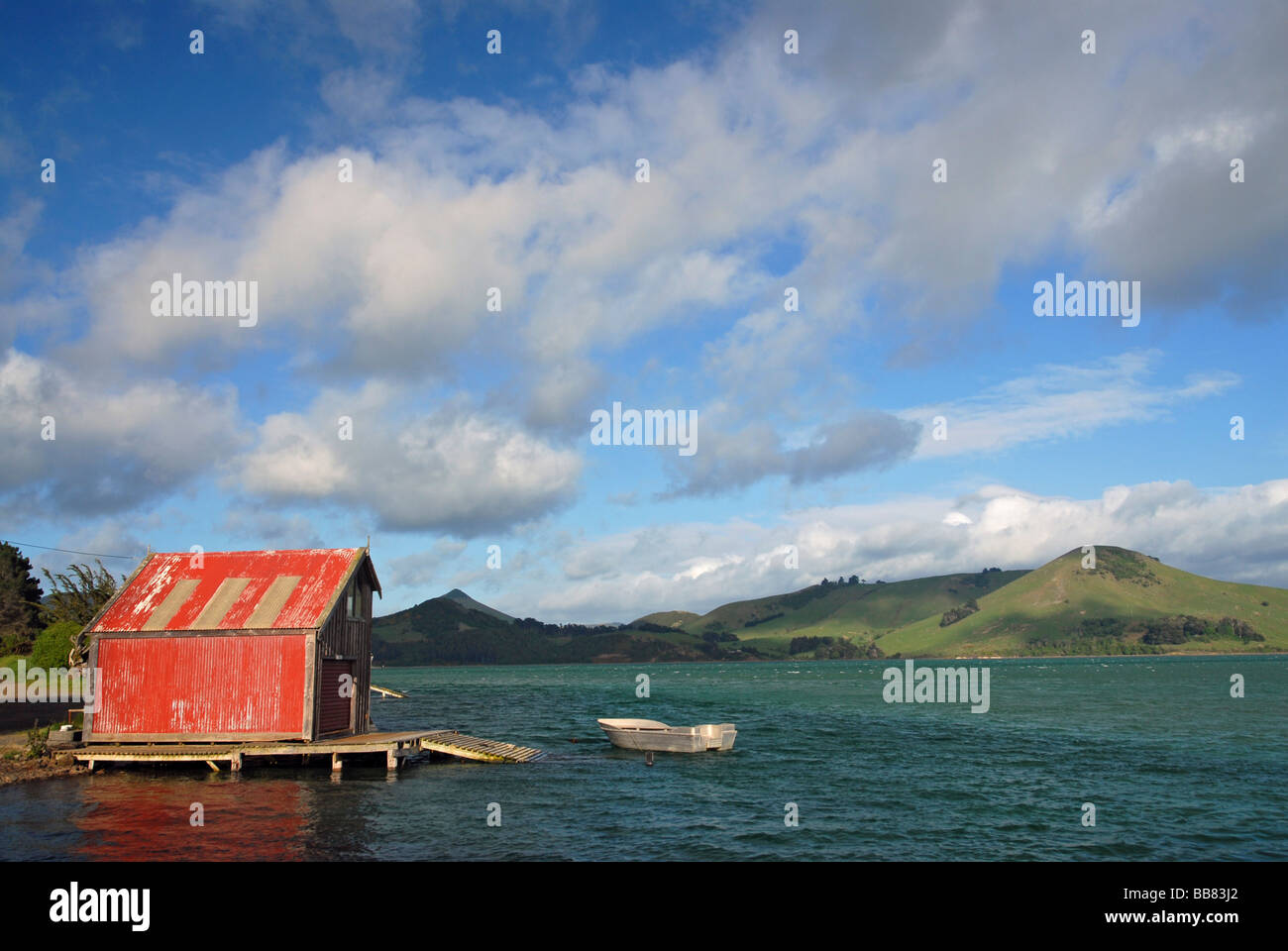 A red boathouse at Papanui Inlet with clouds and Harbour Cone at back ...