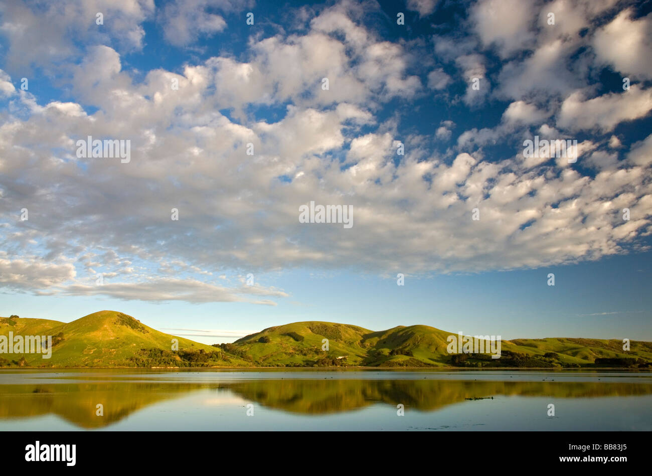 Clouds and rolling green farmland reflected in the calm waters of ...