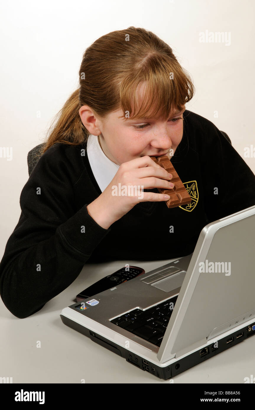 Schoolgirl eating a chocolate bar while using her laptop computer Stock ...