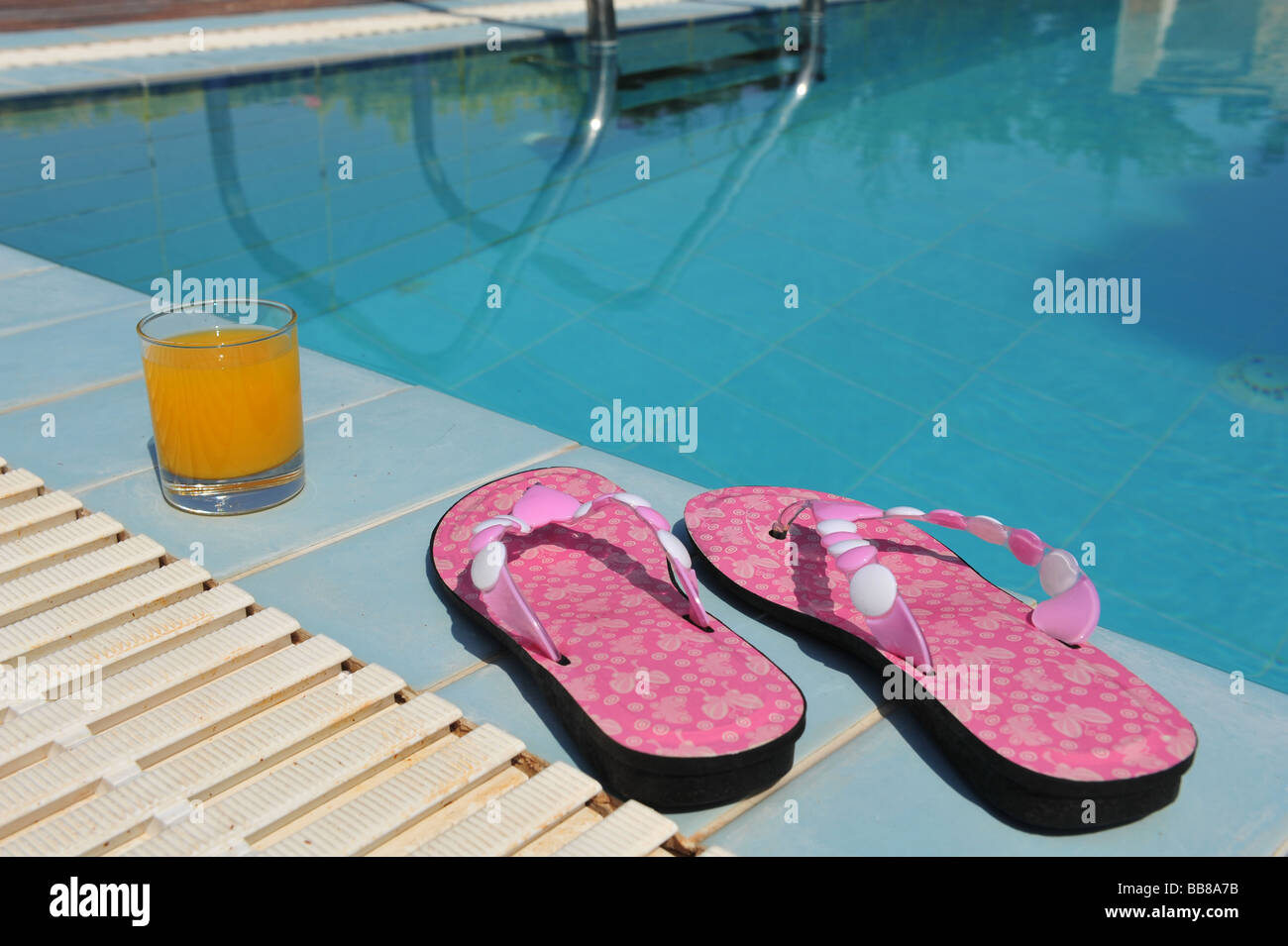 Pair of pink flip flop sandals beside the swimming pool with a glass of orange juice Stock Photo ...