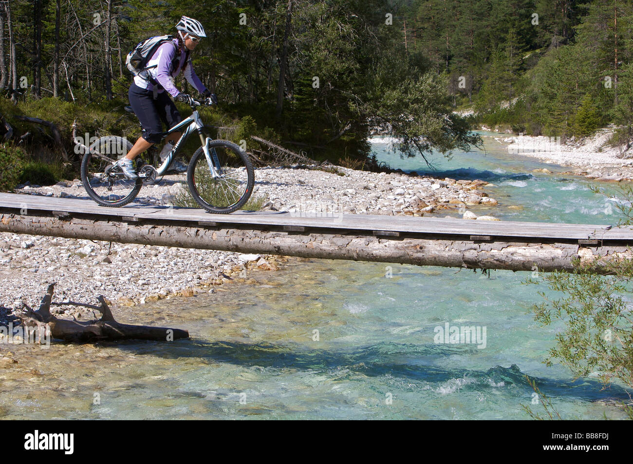 Female mountainbike rider crossing a narrow wooden bridge over the Isar ...