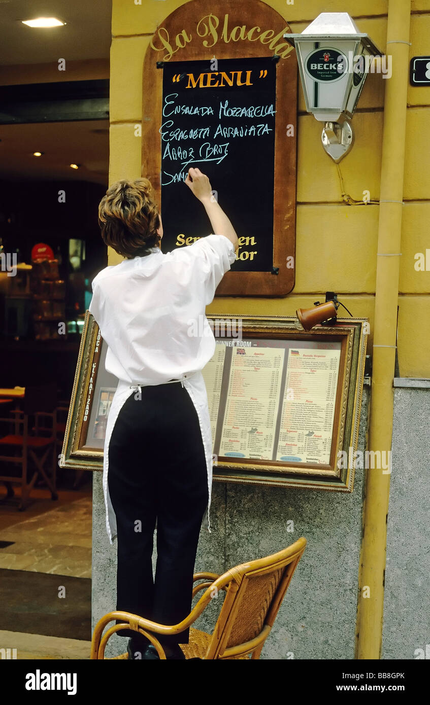 Waitress standing on a chair in front of a restaurant, writing the menu ...