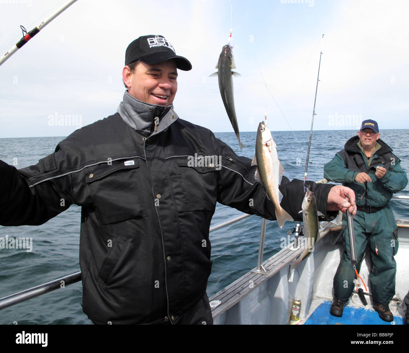 A pleased sport sea fisherman on a boat deck displays his catch 3 small ...