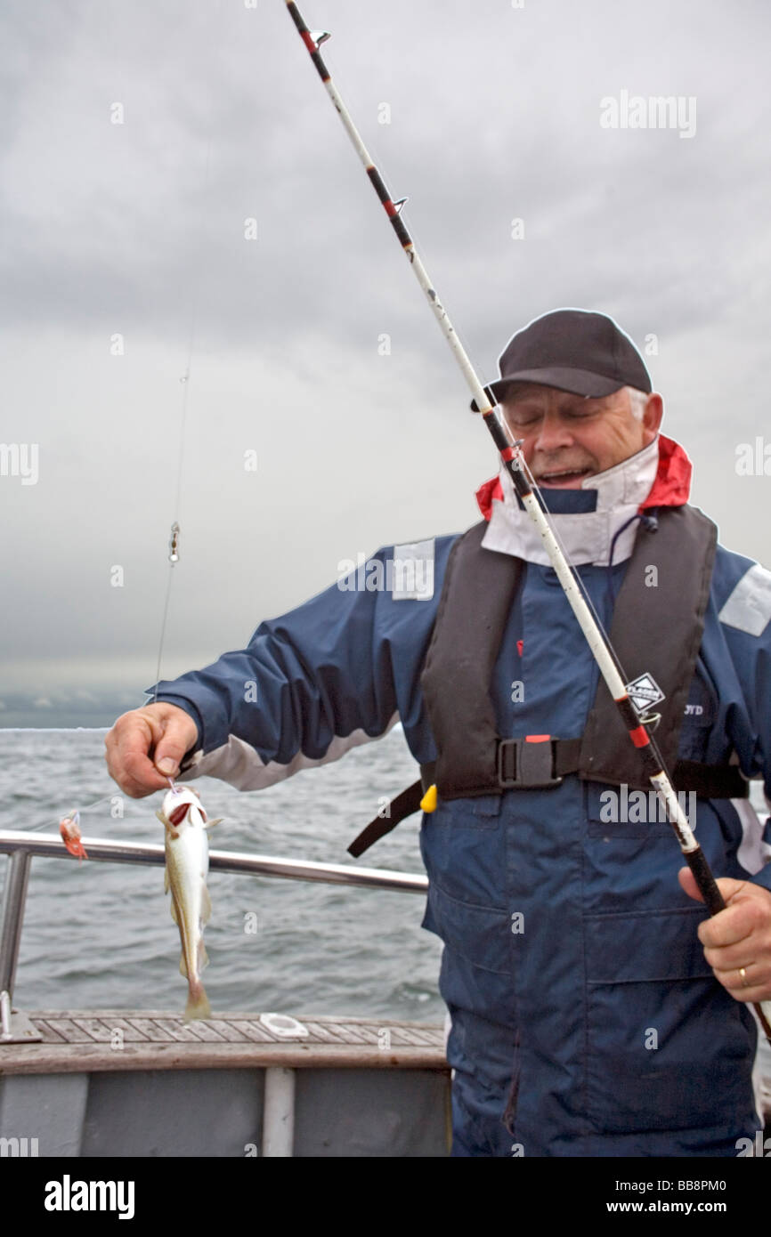 A pleased sport sea fisherman on a boat deck displays his catch a small ...