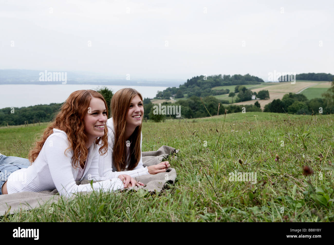 Two teenagers smiling lying on a field with lake view Stock Photo - Alamy