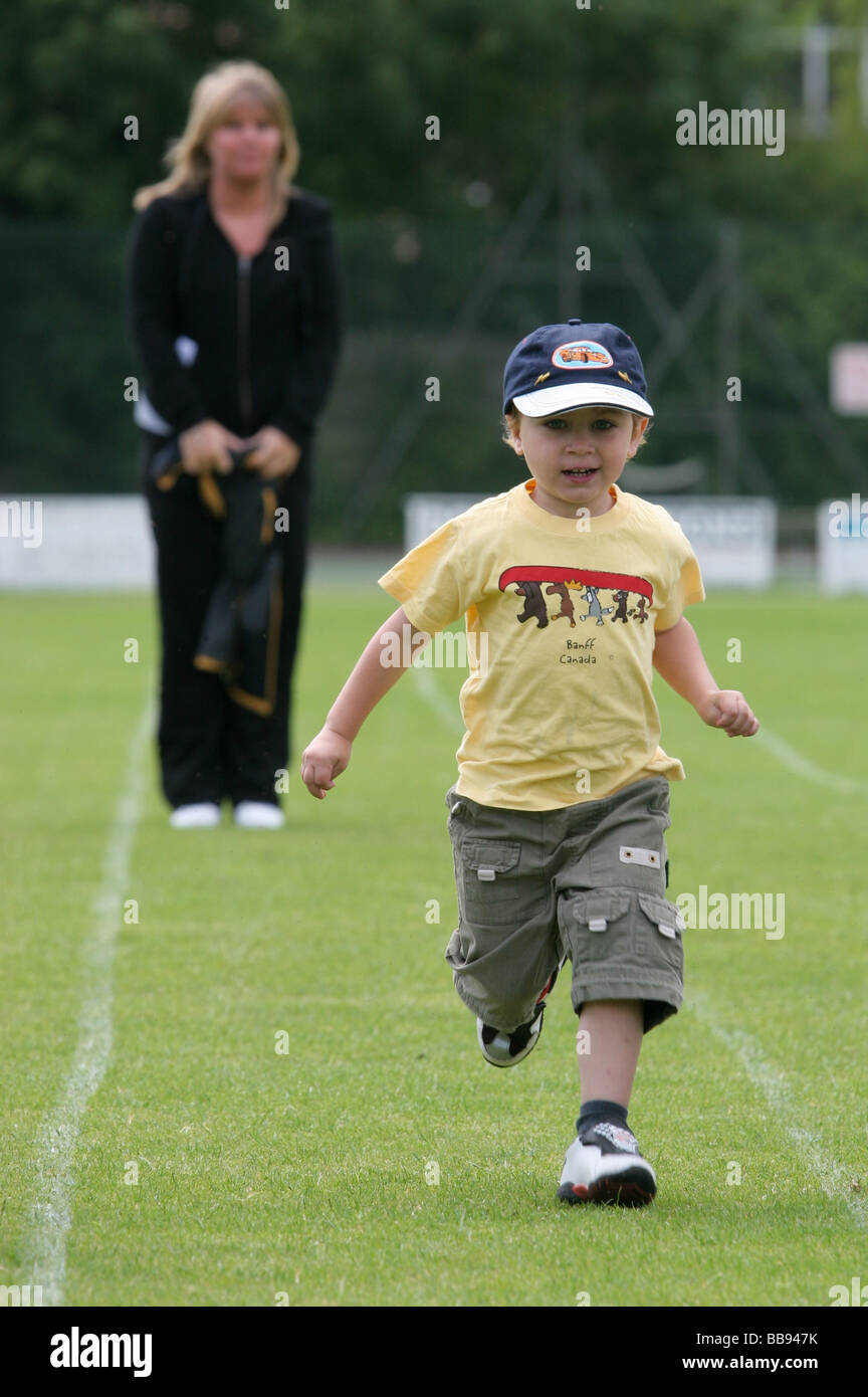 Boy running in track on grass field on school sports day with teacher ...