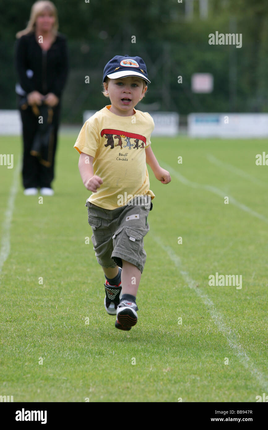 Boy running in track on grass field on school sports day with teacher ...