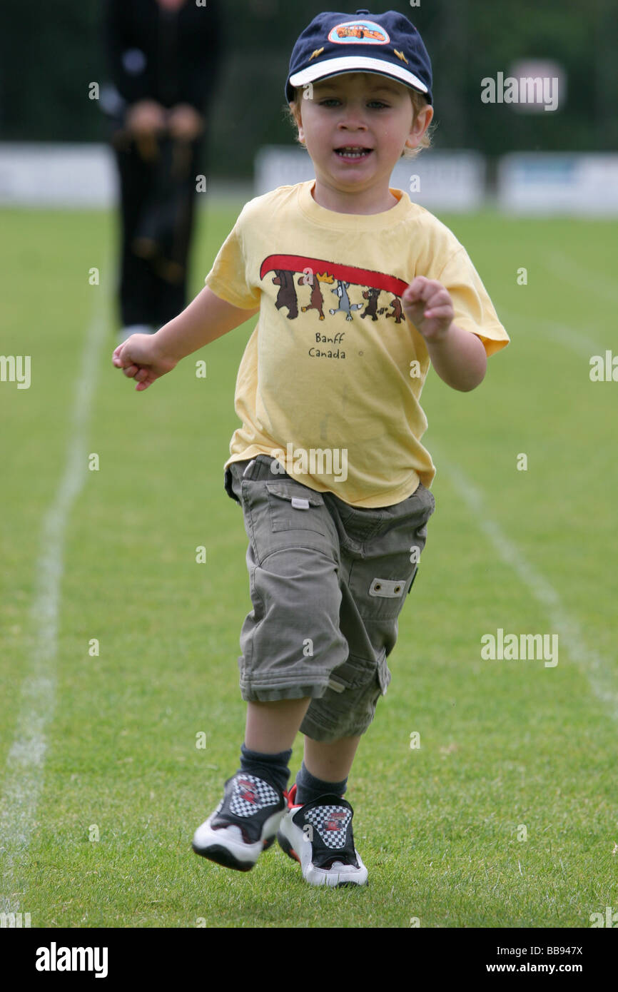 Boy running in track on grass field on school sports day with teacher ...