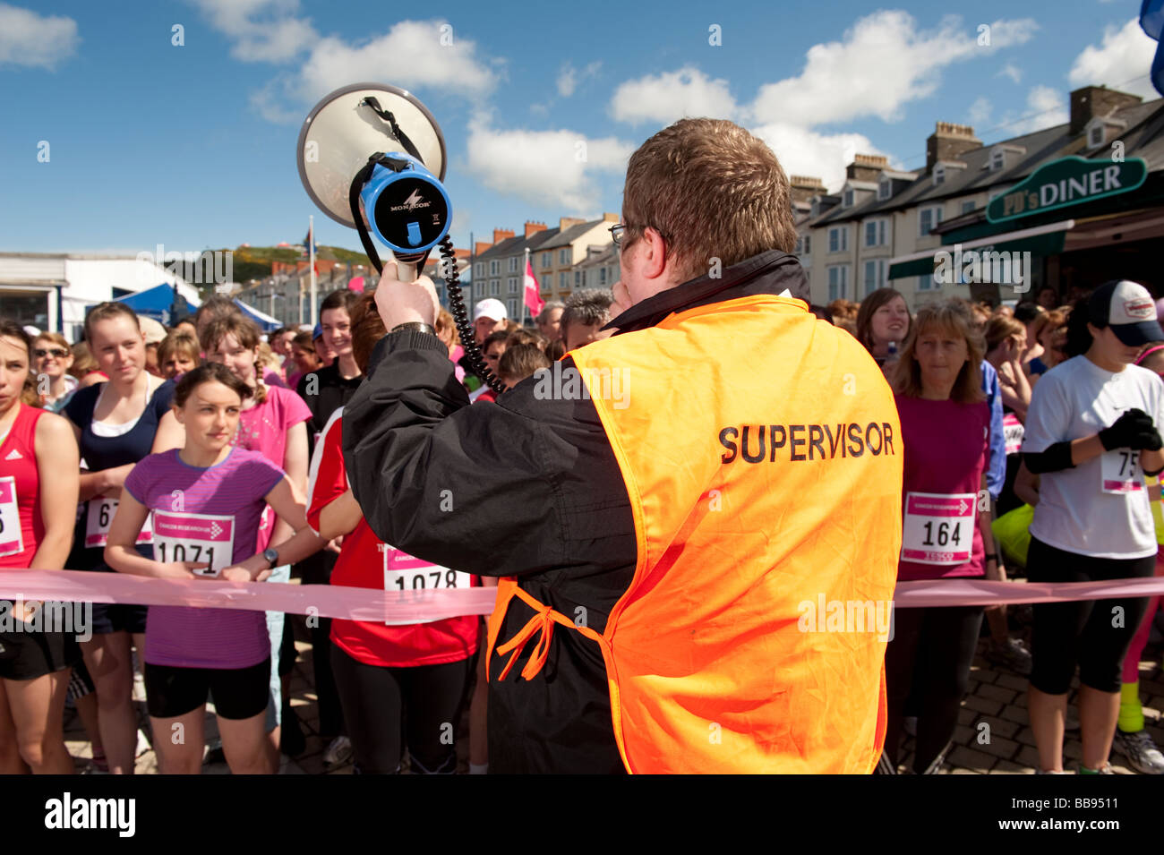 Male supervisor wearing orange tabard holding a megaphone giving ...