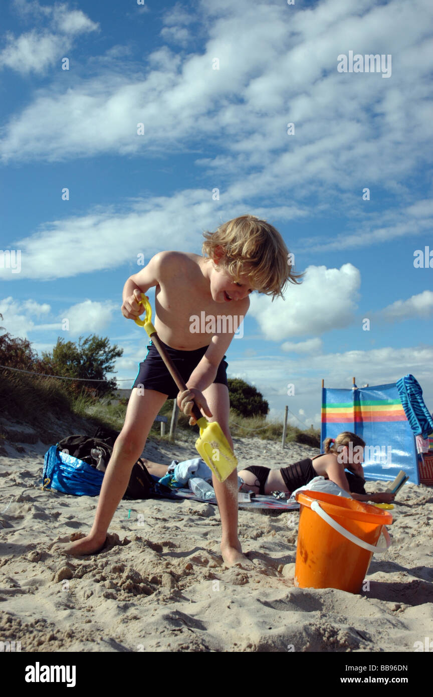 Young boy shovelling sand on the beach Stock Photo - Alamy
