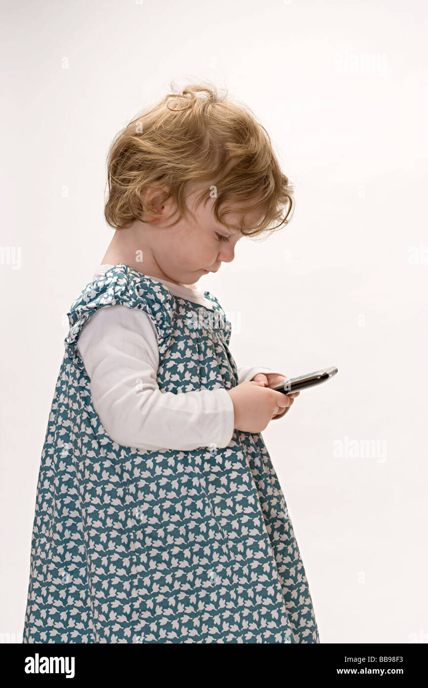 baby girl standing up looking at an iphone that's she's holding in her ...