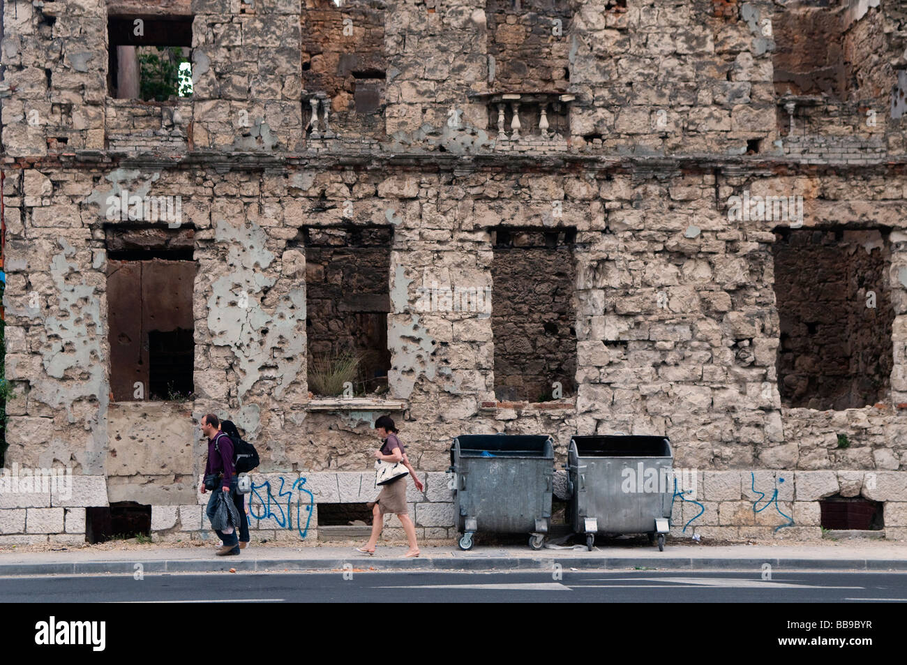 Pedestrians walk past a house showing shrapnel damage from the 1992-95 ...
