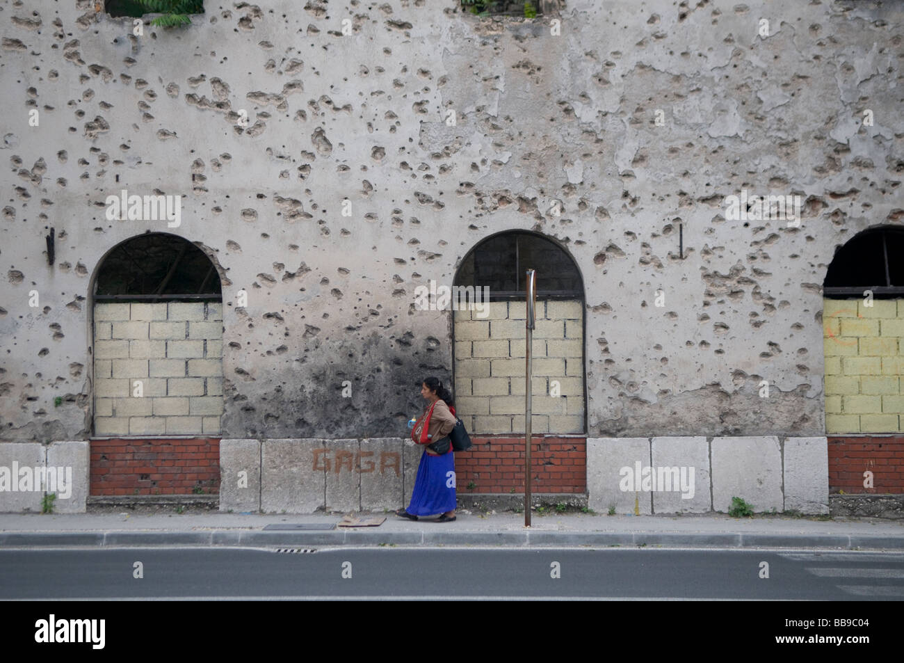 A gypsy woman walks past a building riddled with bullet holes from the ...