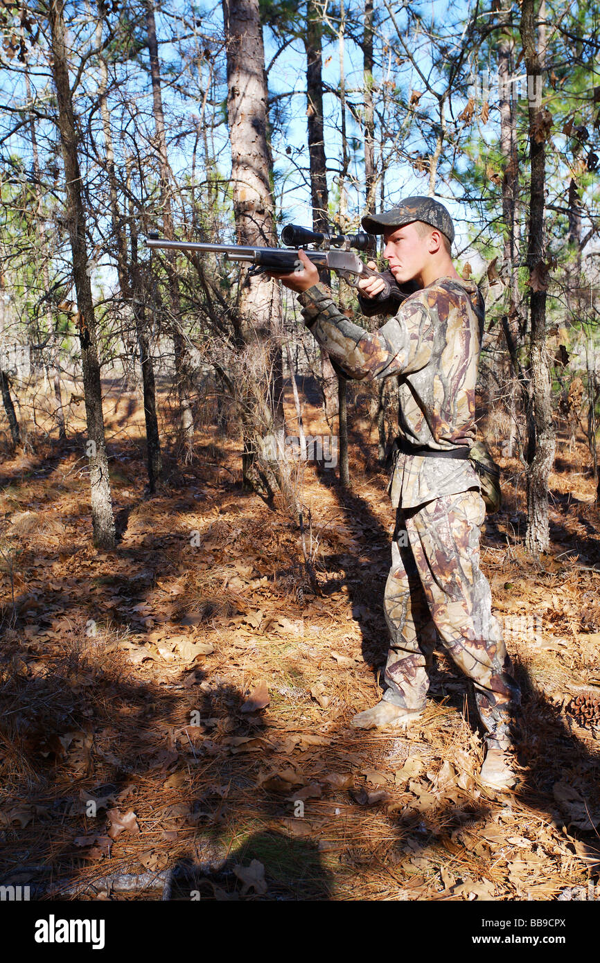 CLOSE UP HUNTER AIMING WEAPON STANDING IN A PINE FOREST LOOKING ...