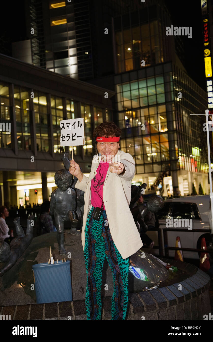 Eccentric man holding up a sign that reads SMILE THERAPY in Japanese ...