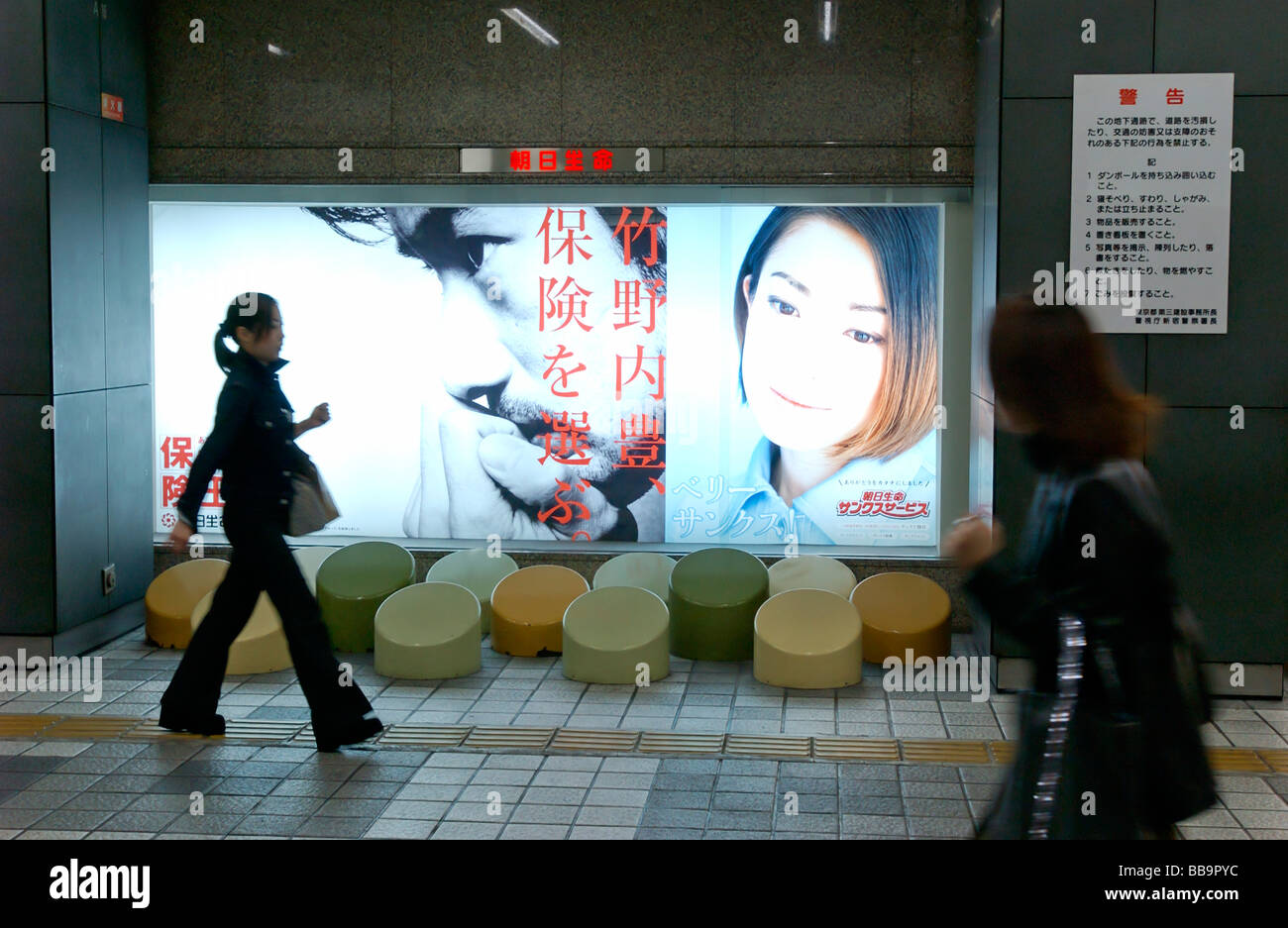 Two Japanese women in front of an underground advertisement, Shinjuku ...