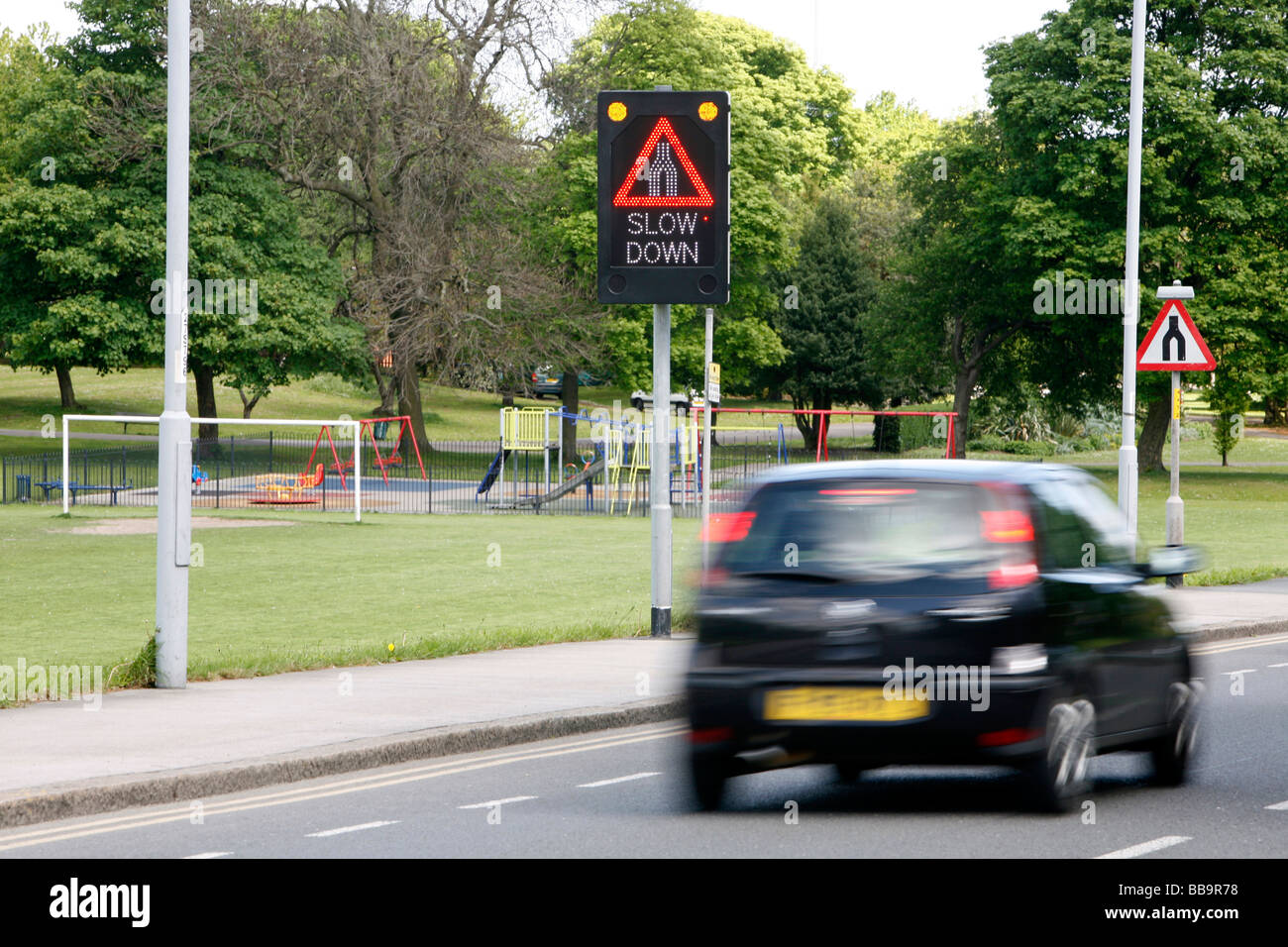 Illuminated converging lanes slow down sign at side of road Stock Photo ...