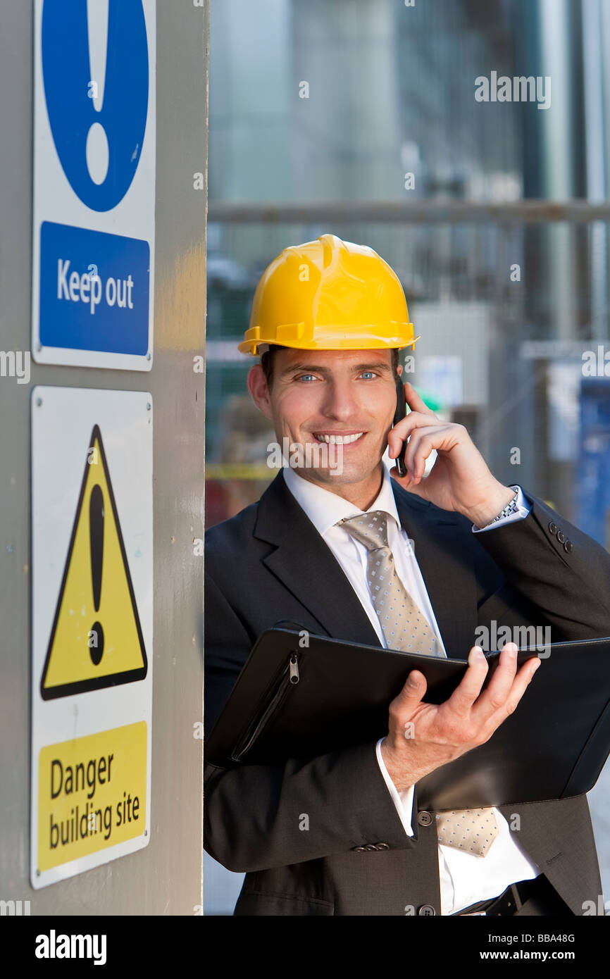 A male manager on a construction site wearing a hard hat and talking on ...