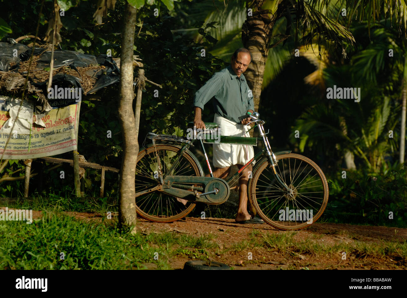 India, Kerala, backwaters. Indian man pushing his bicycle along a canal ...