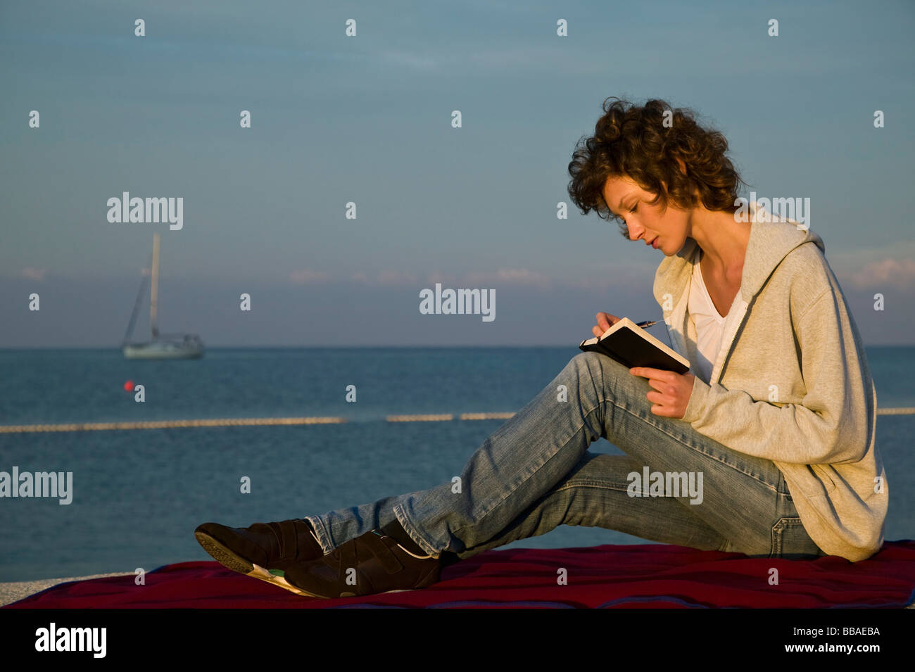 A woman sitting near the sea writing in a journal Stock Photo - Alamy
