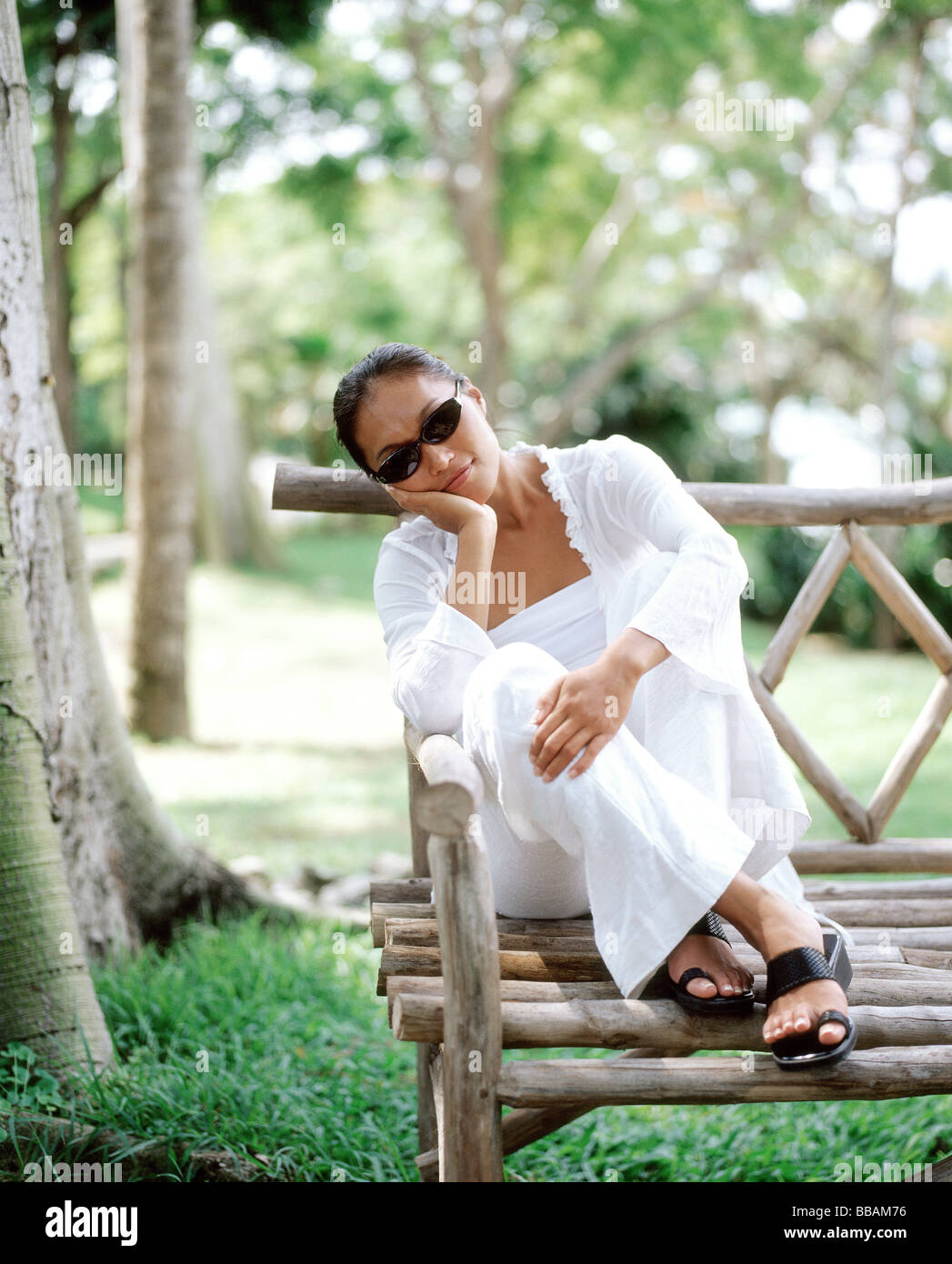 Woman sitting on wooden bench, trees behind Stock Photo - Alamy