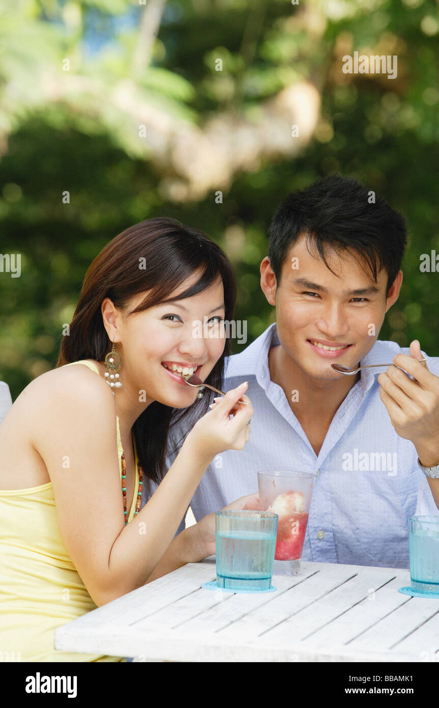 Couple sitting side by side, eating, smiling at camera Stock Photo - Alamy