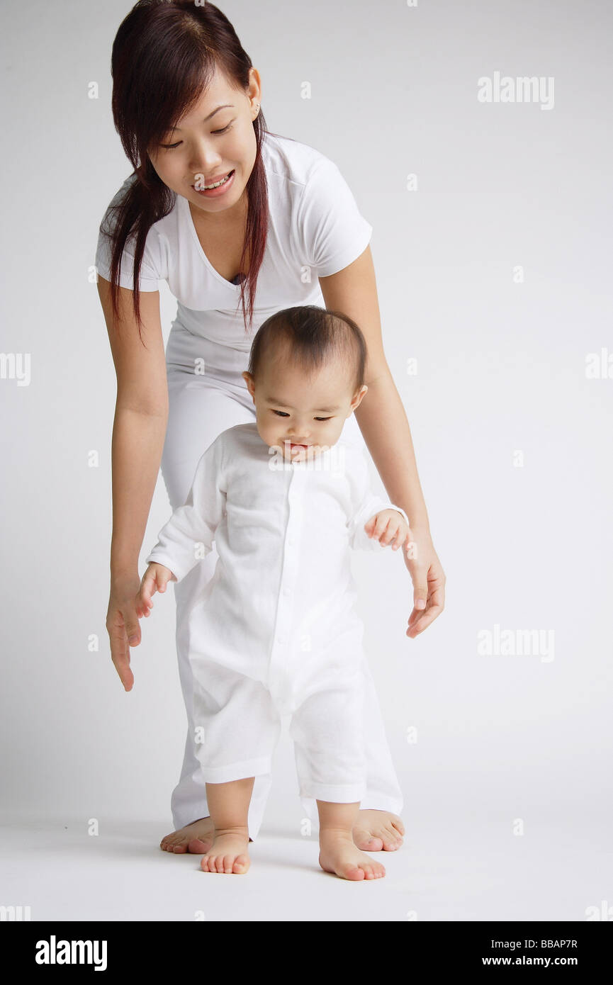Baby girl standing, mother behind her Stock Photo - Alamy