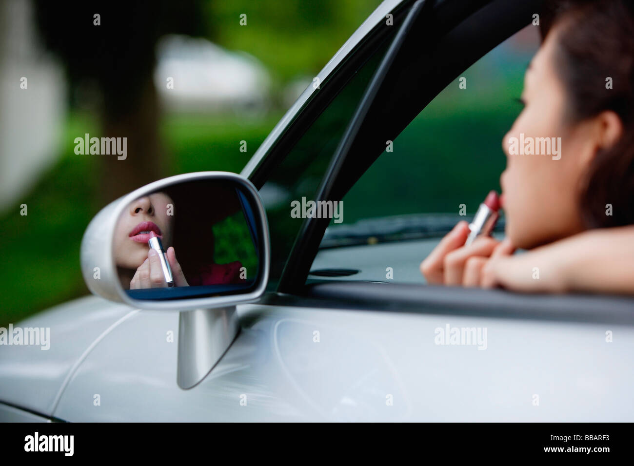 Woman applying lipstick in side view mirror of car, while in driver's ...