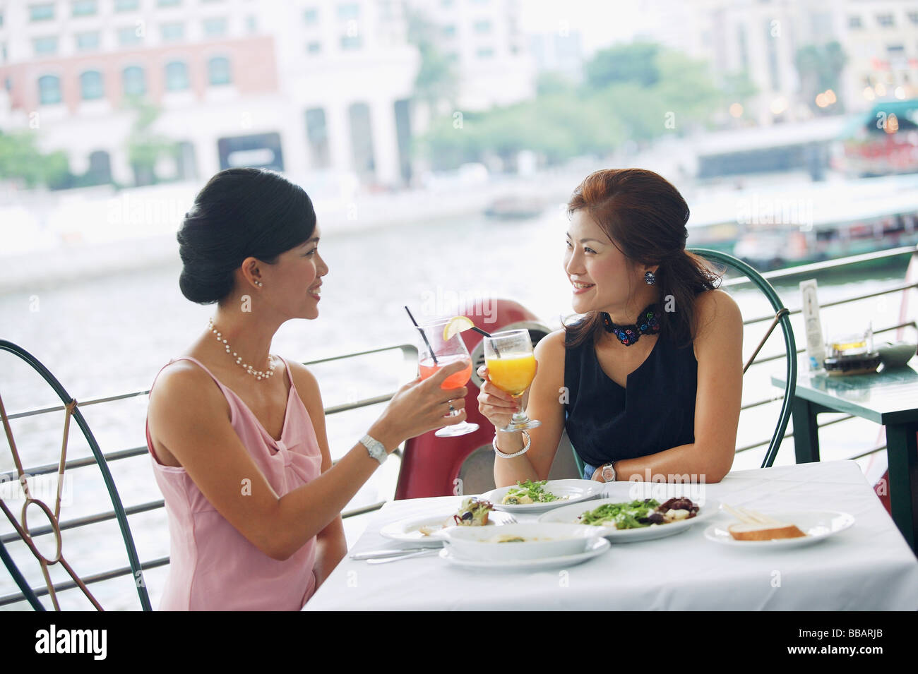 Two women having lunch, toasting with drinks Stock Photo - Alamy