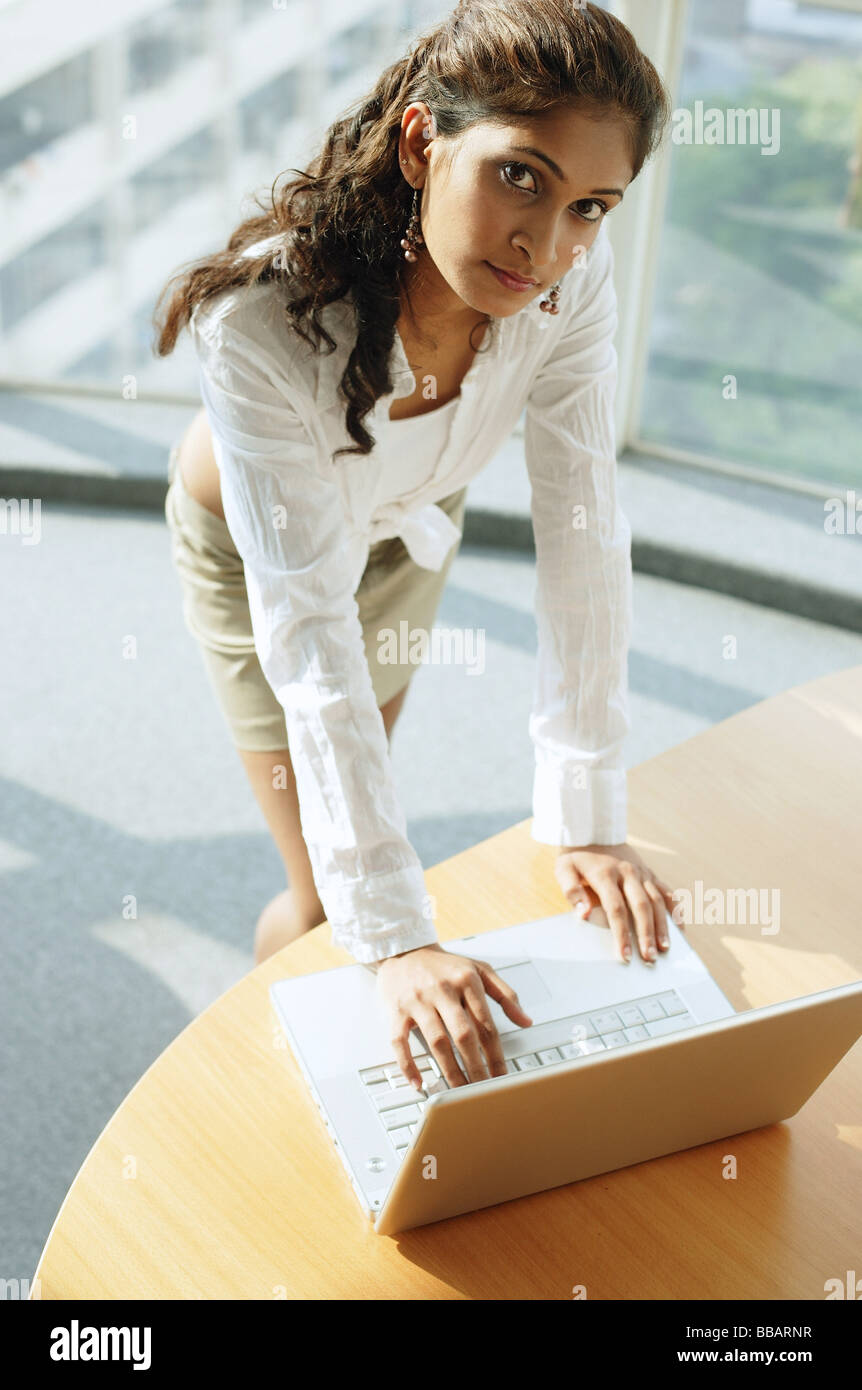 Woman standing over desk, using laptop, looking up at camera Stock ...