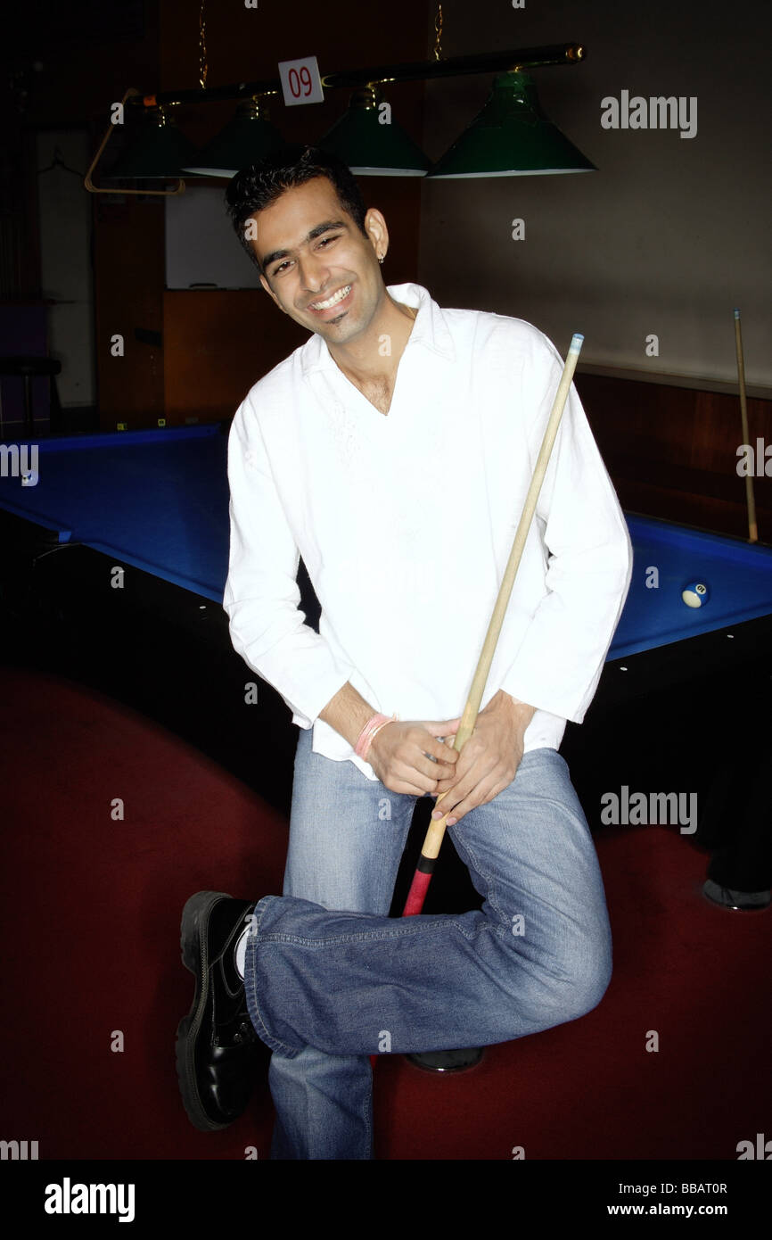 Young man leaning against pool table, holding pool cue Stock Photo - Alamy