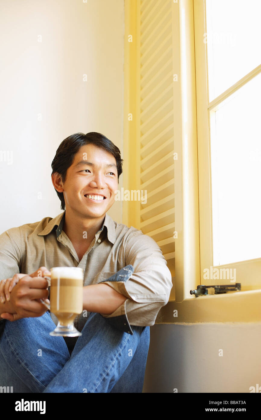 Man sitting next to window holding mug of coffee Stock Photo - Alamy