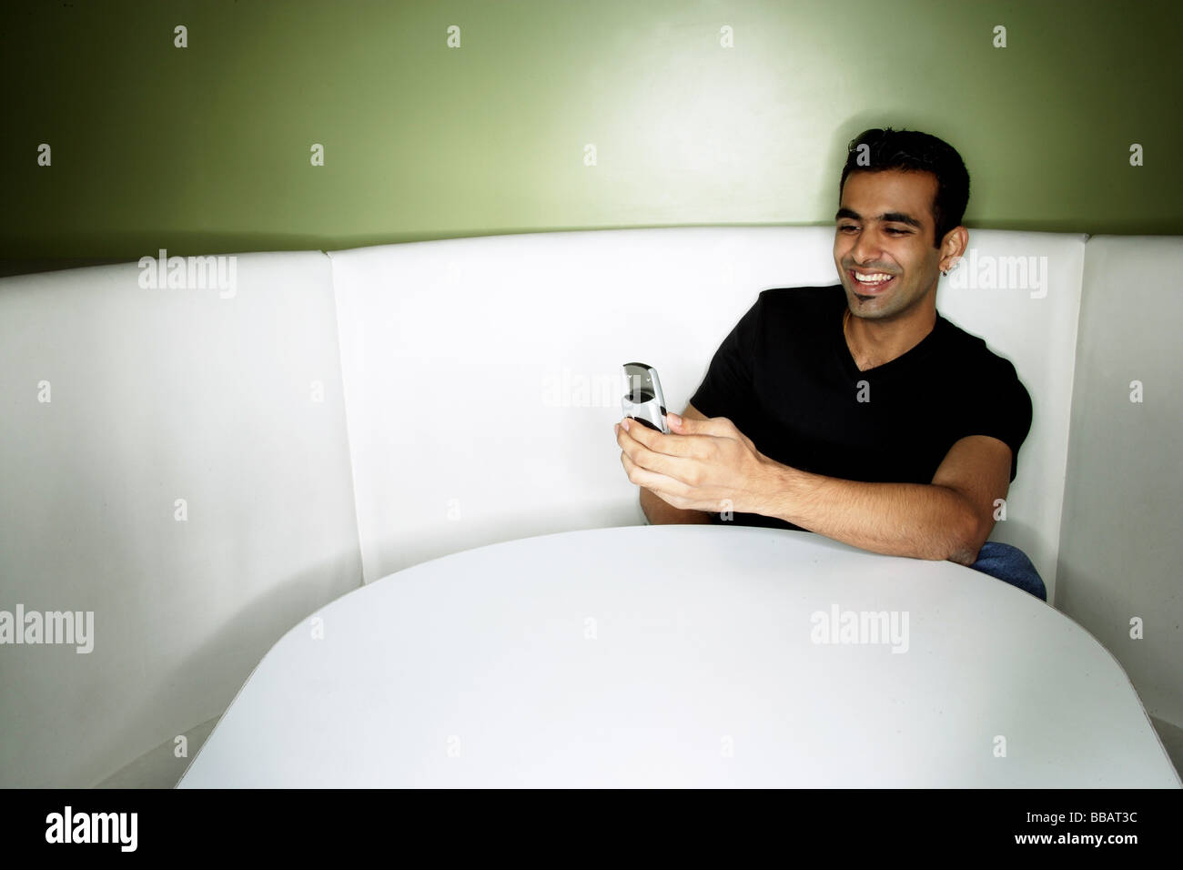 Young man sitting in booth, looking at mobile phone Stock Photo - Alamy