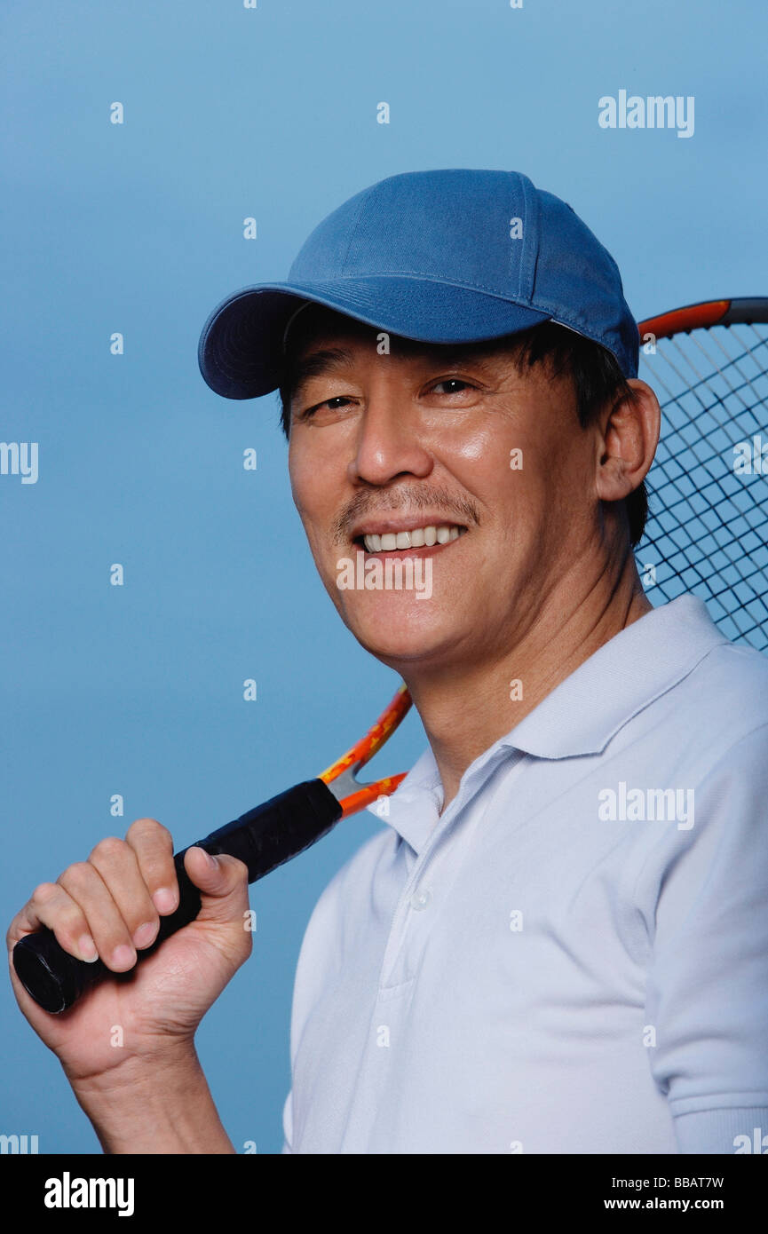 Man holding tennis racket over shoulder, smiling at camera Stock Photo ...