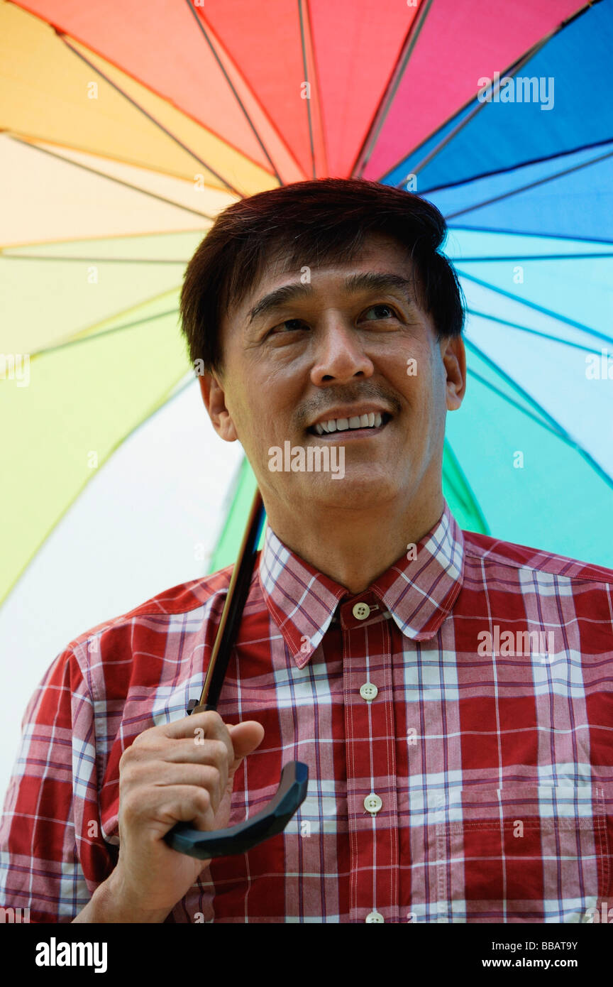 Man standing under rainbow umbrella, smiling Stock Photo - Alamy