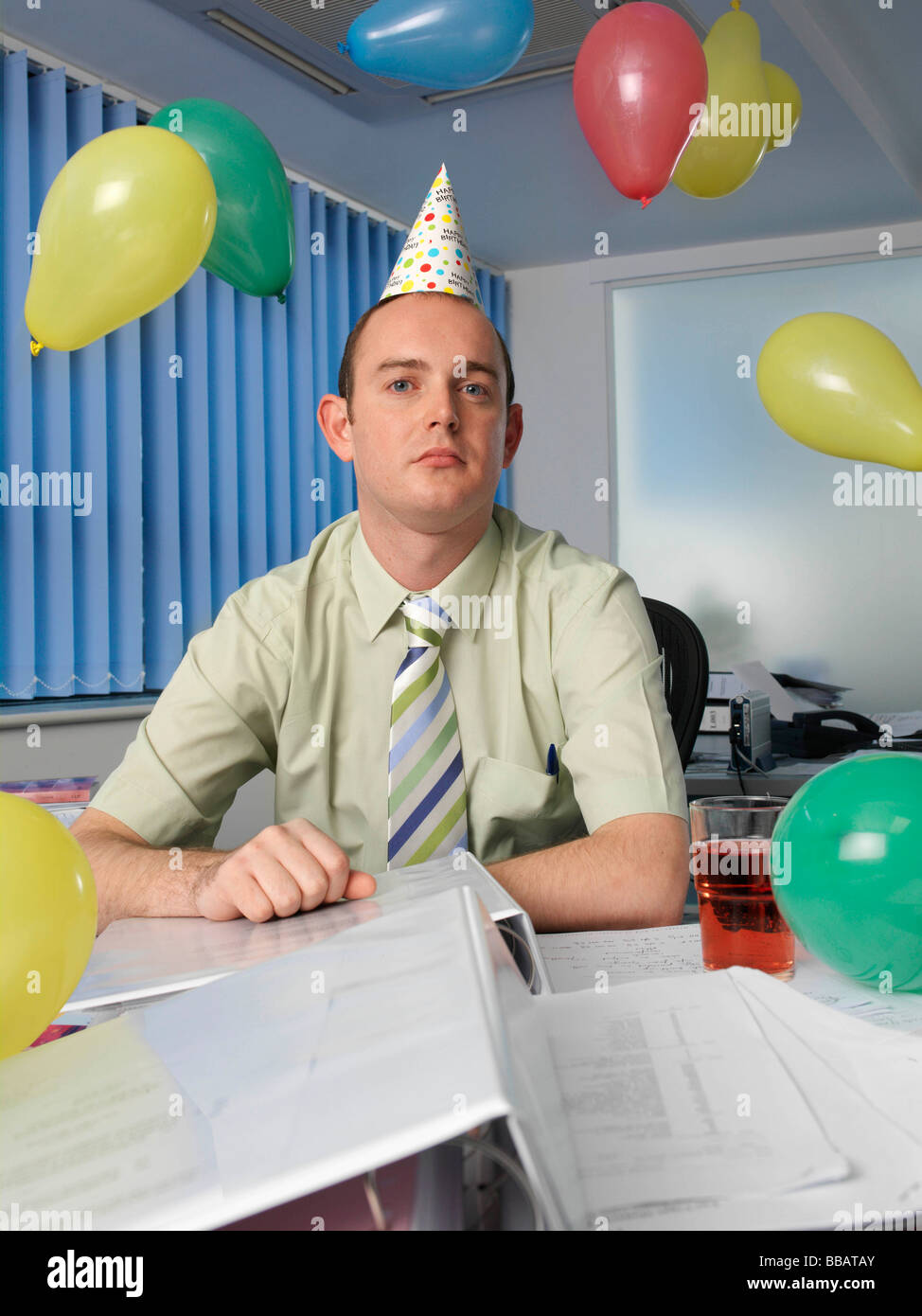 Grumpy office worker in party hat Stock Photo - Alamy