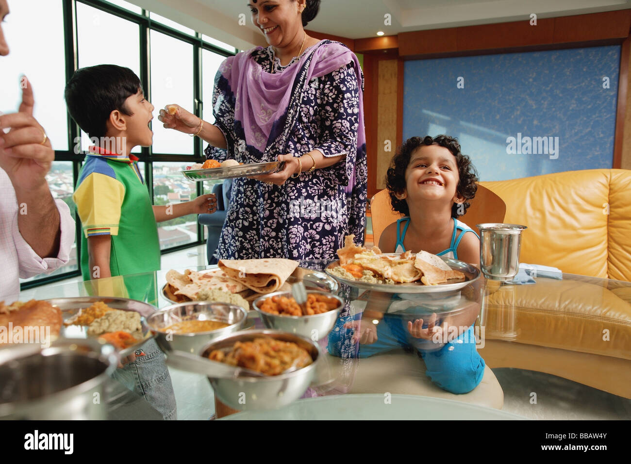 Family of four having a meal at home, mother feeding son Stock Photo ...