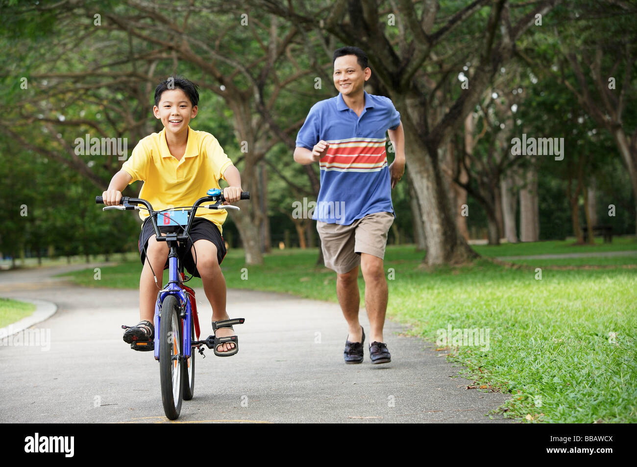 Boy cycling, father running behind him Stock Photo - Alamy